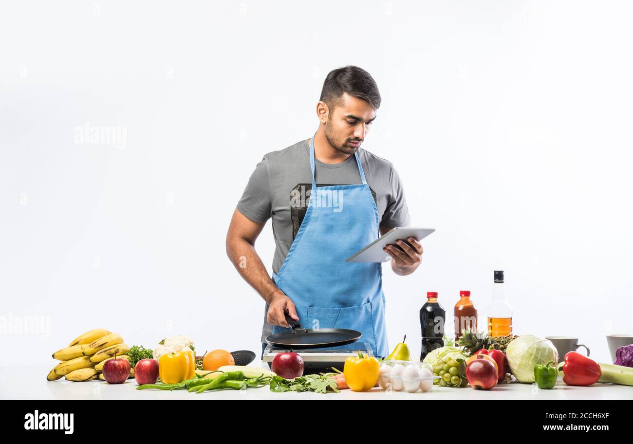 Handsome cheerful smiling indian man preparing meal in the kitchen ...