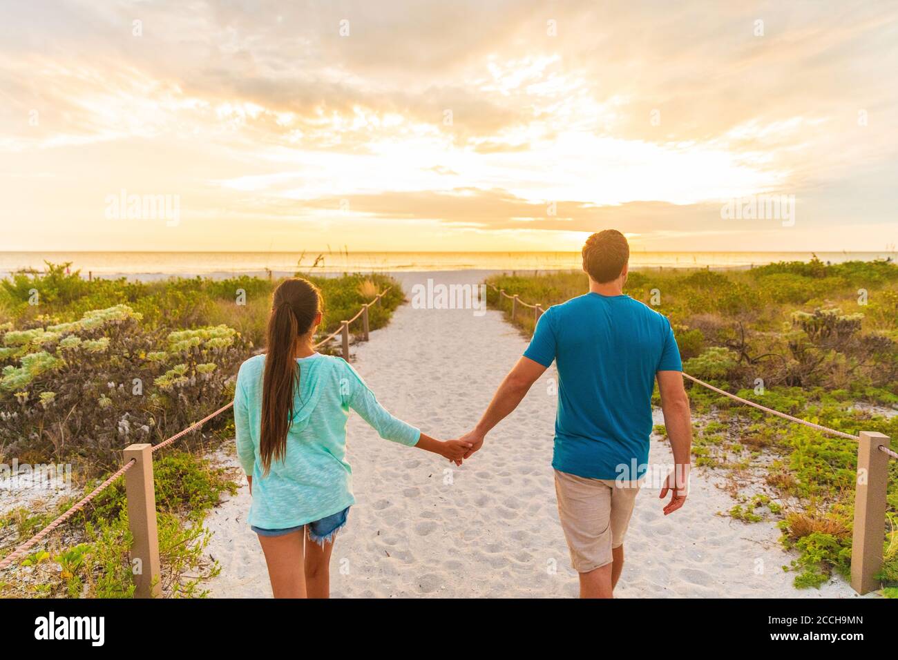 Happy Young Couple In Love Walking On Romantic Evening Beach Stroll At