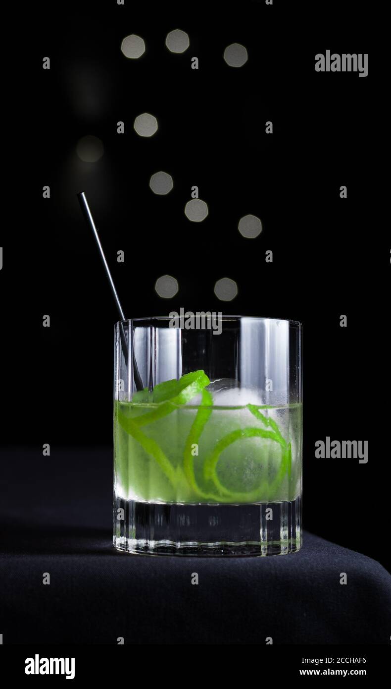Craft cocktail in rocks glass with ice sphere and lime garnish isolated ...