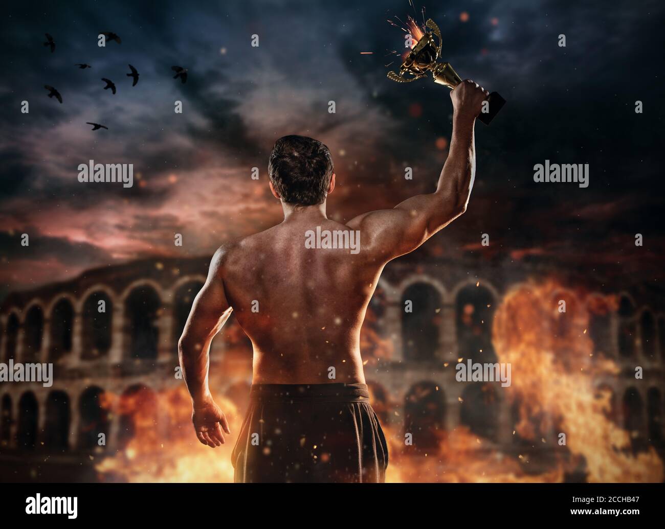 Back view of muscular man holding burning trophy cup, antique colosseum ...