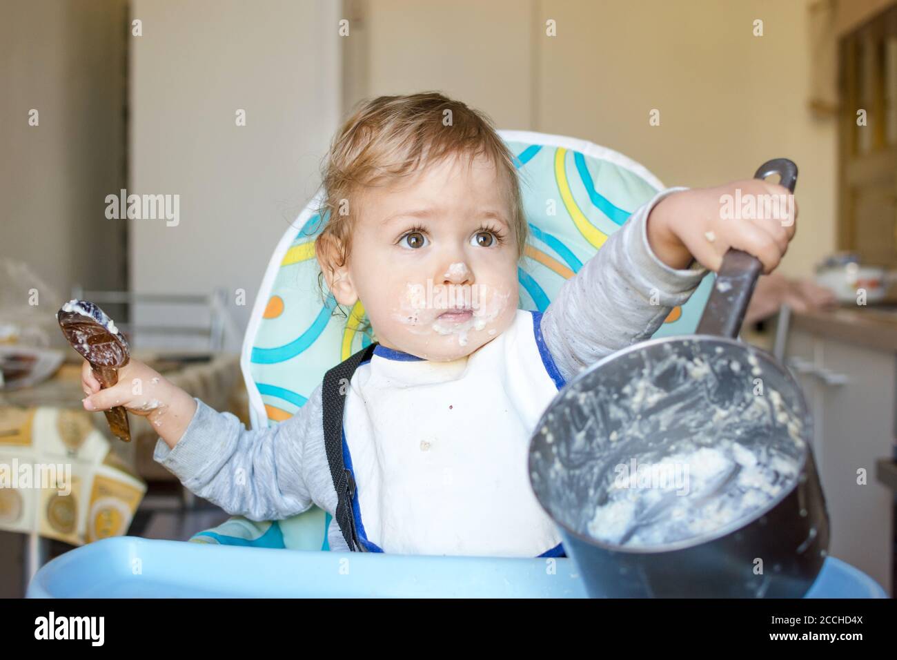 Funny baby child getting messy eating cereals or porridge by itself ...