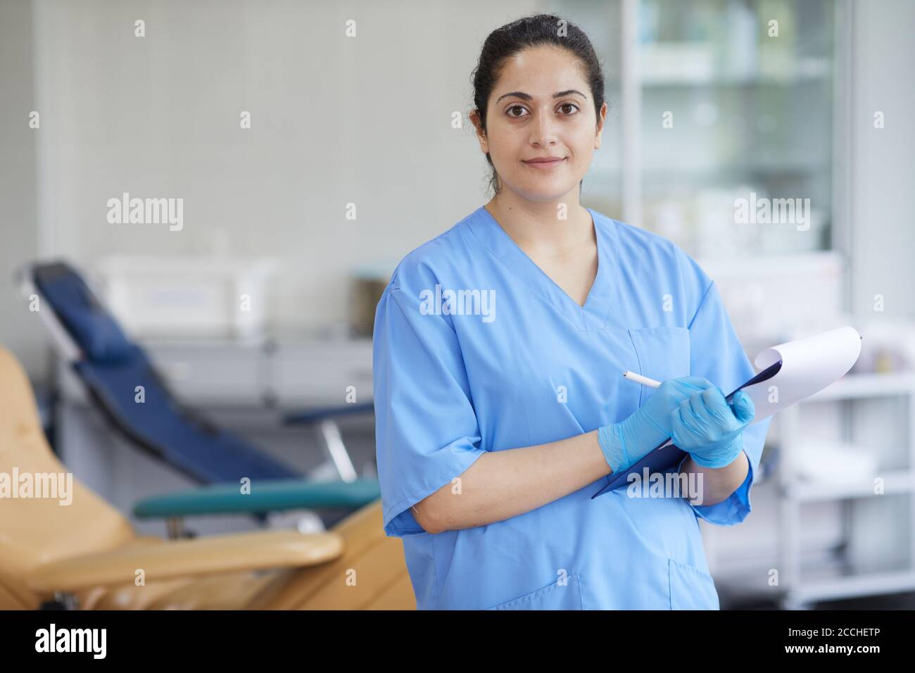 Portrait of nurse in uniform looking at camera while writing in medical ...