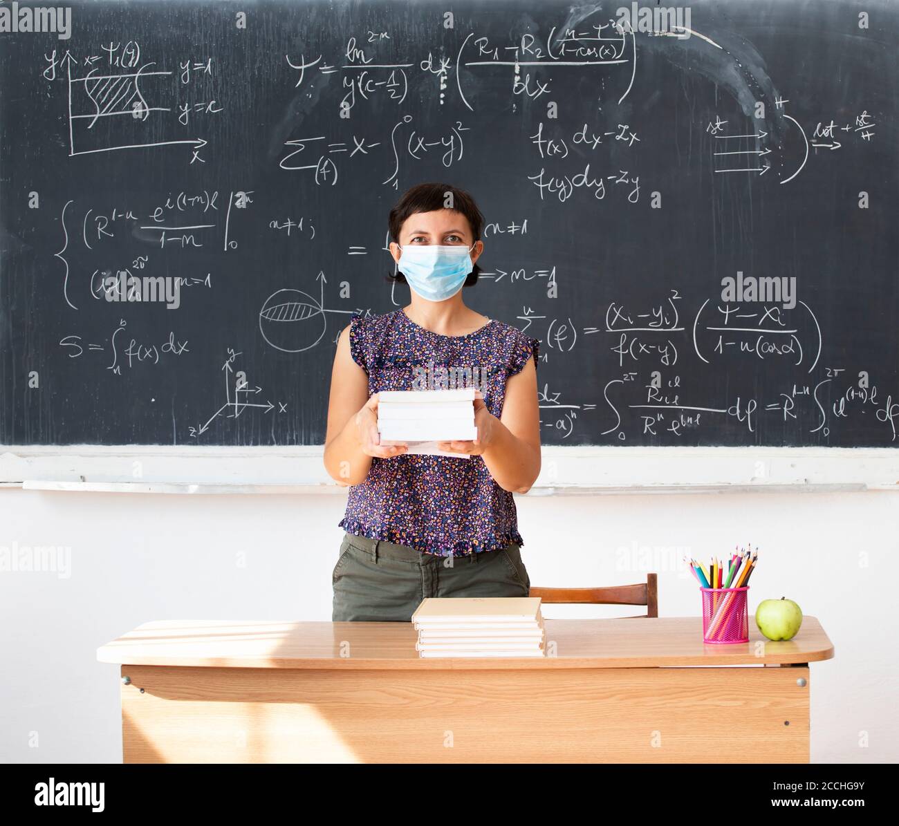 Teacher with face mask welcoming children back at school after lockdown ...