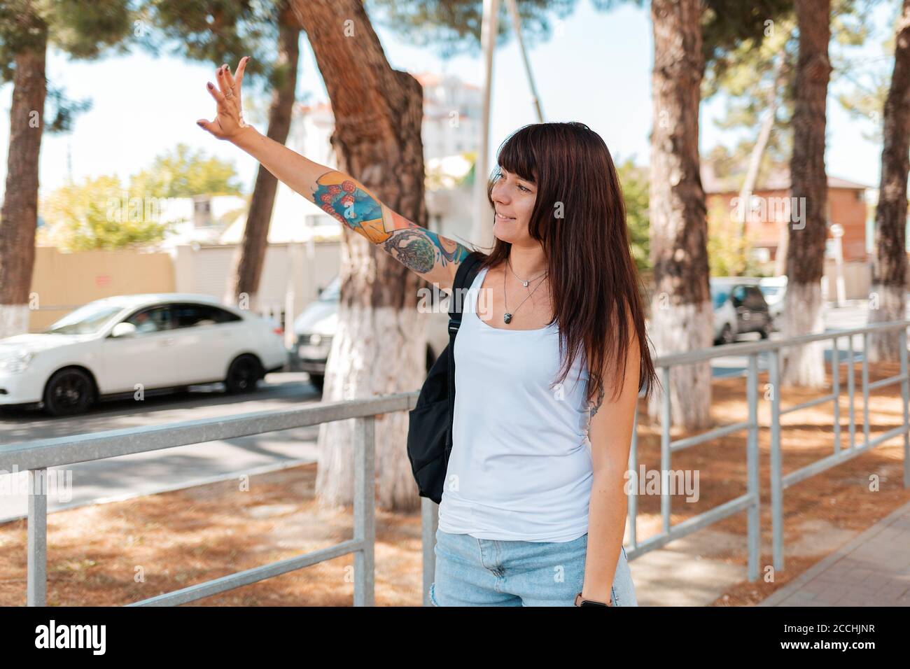 Summertime. A woman walks down the street and joyfully waves to someone ...