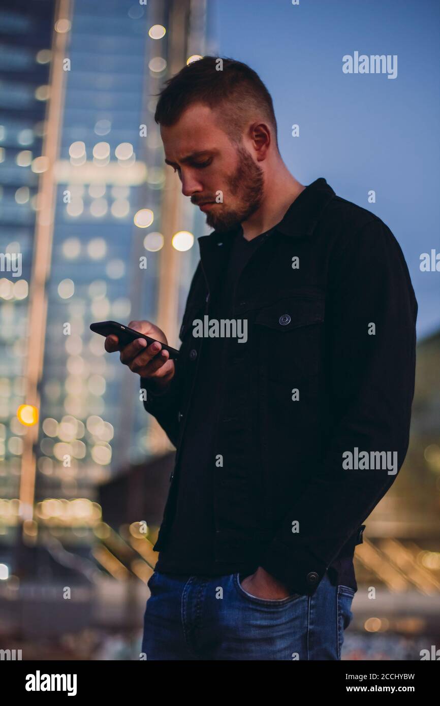 Man using smartphone texting. Male standing in the city in the evening ...