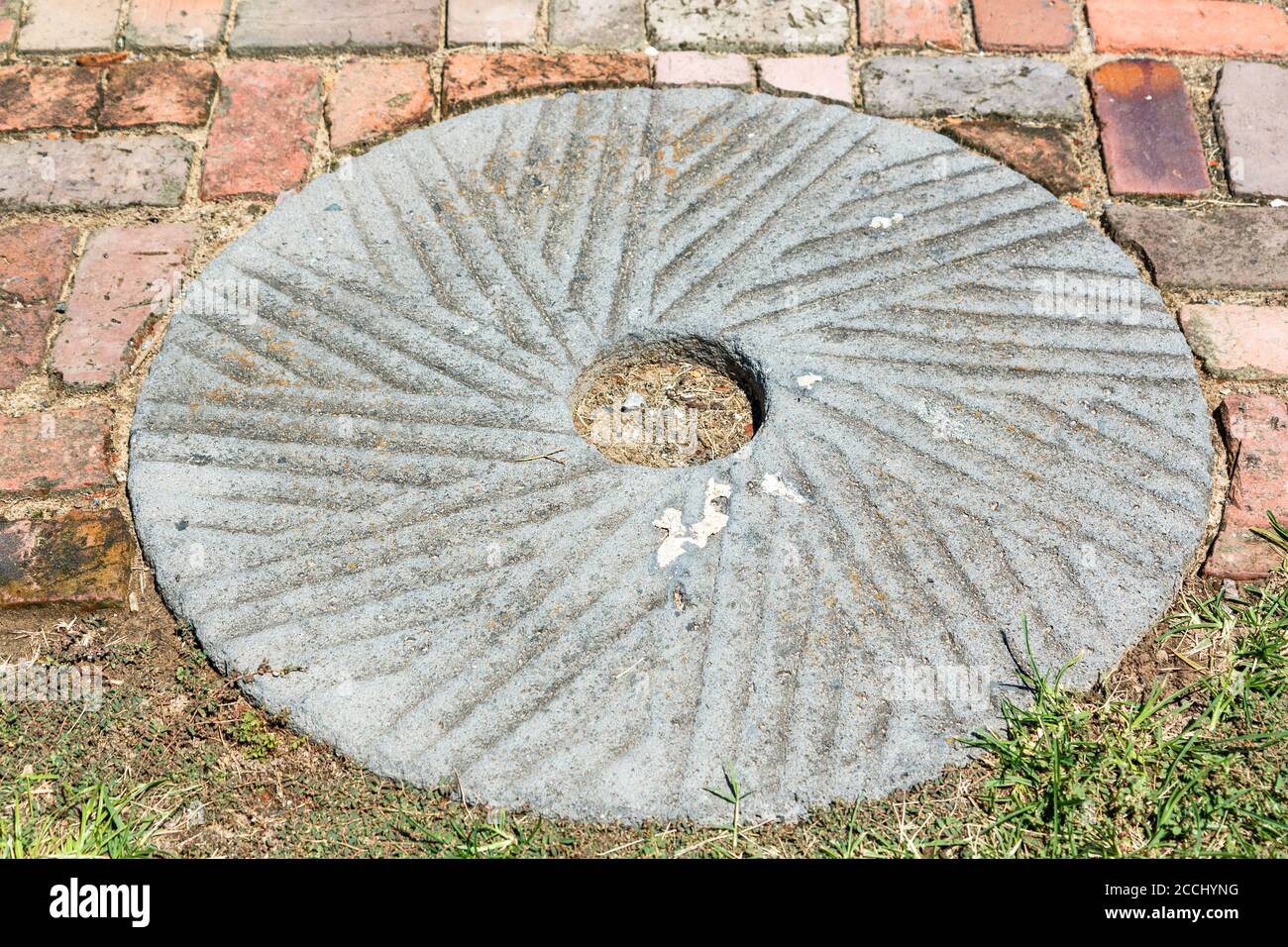 Millstone set in brick and grass to be used as lawn art Stock Photo - Alamy