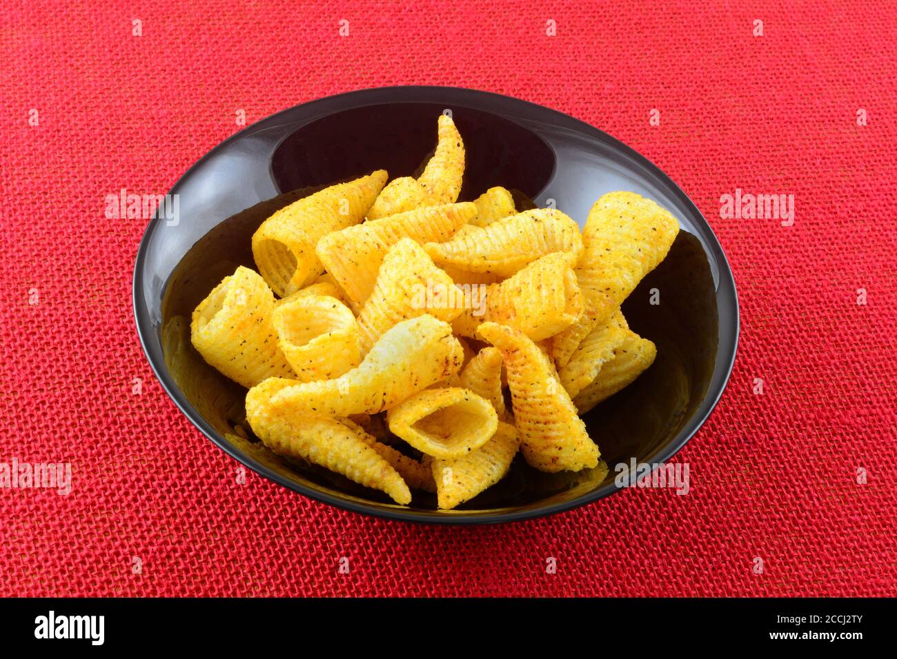 Pizza flavored cone shaped corn snacks in black bow on red tablecloth ...