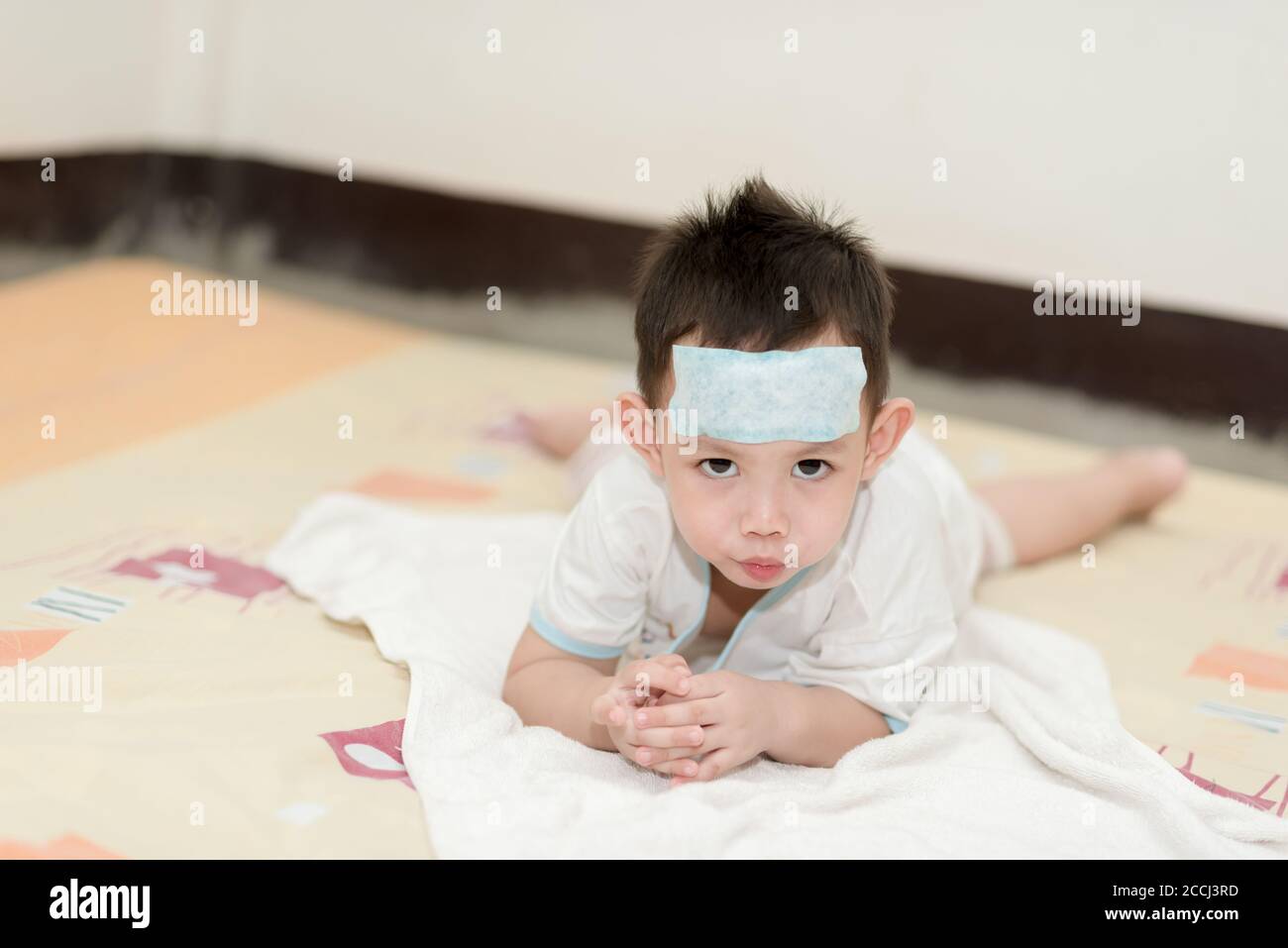 Asian boy having fever . The kid attach cooling gel pad on his forehead ...