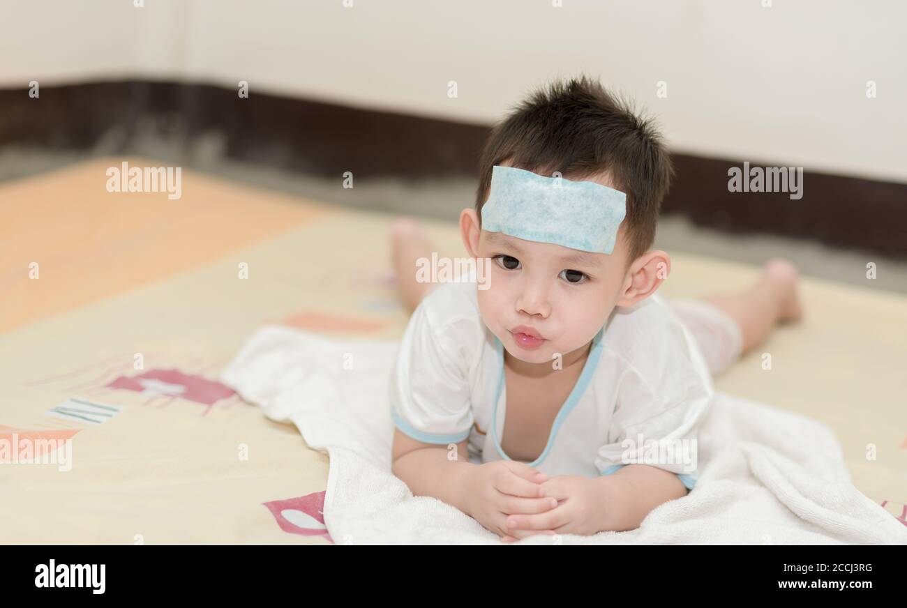Asian boy having fever . The kid attach cooling gel pad on his forehead ...