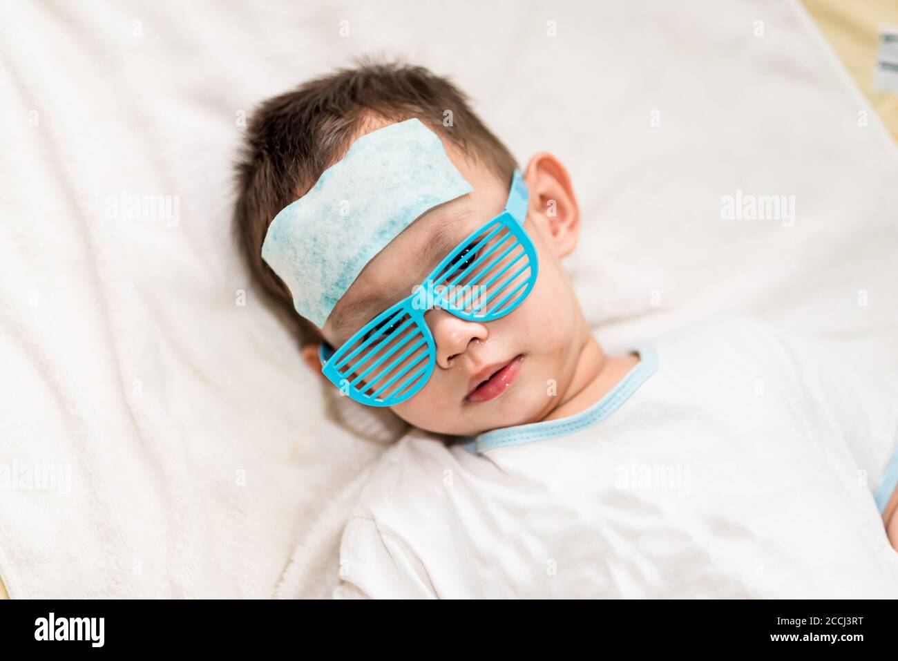 Asian boy having fever . The kid attach cooling gel pad on his forehead ...