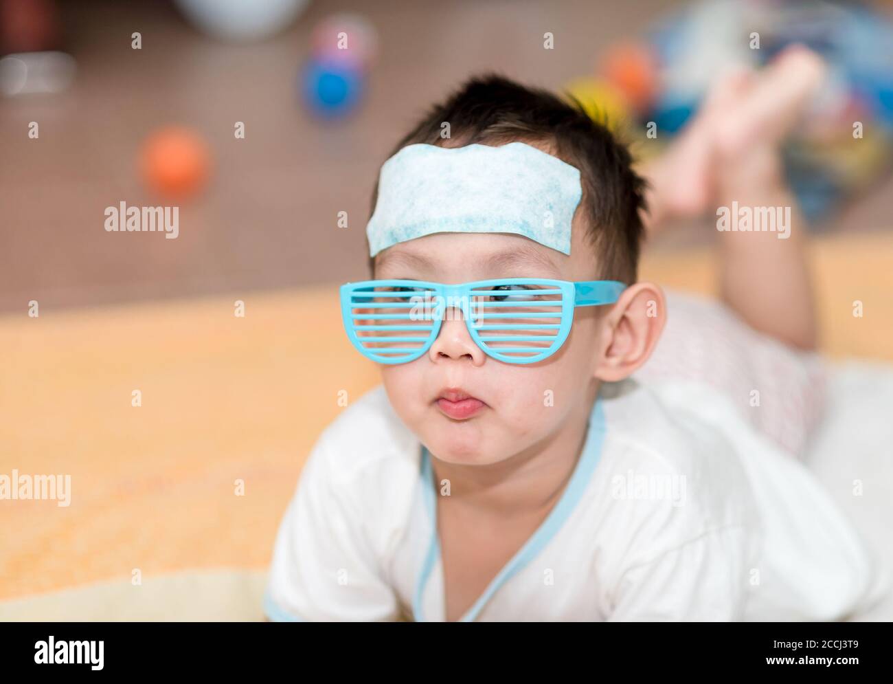 Asian boy having fever . The kid attach cooling gel pad on his forehead ...