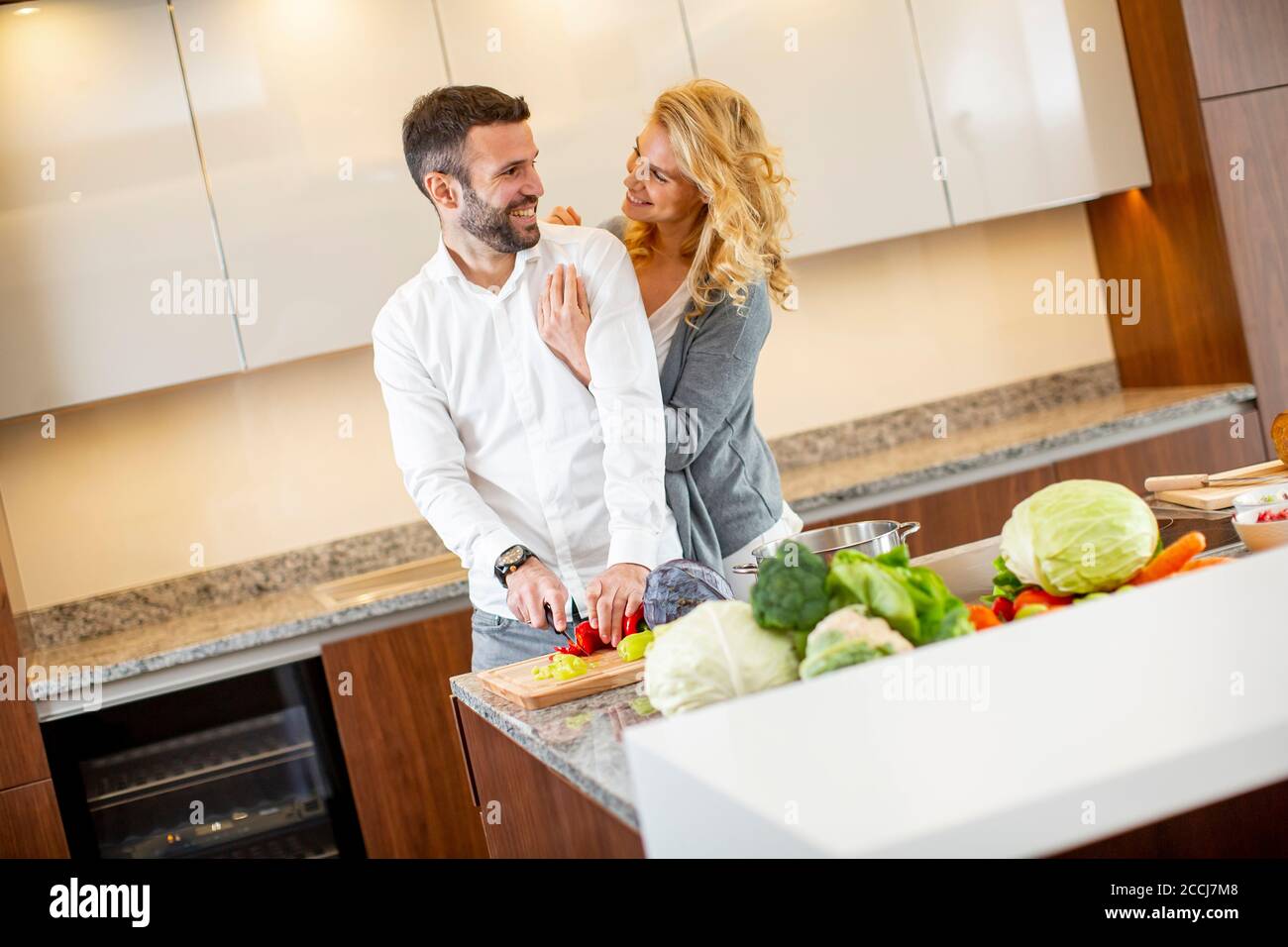 View at young man helping his girlfriend cooking in modern kitchen ...