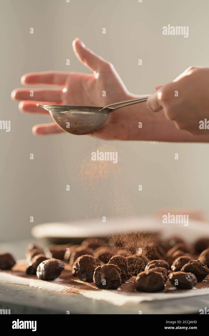 young female hands sprinkle fresh chocolate truffles with cocoa powder ...