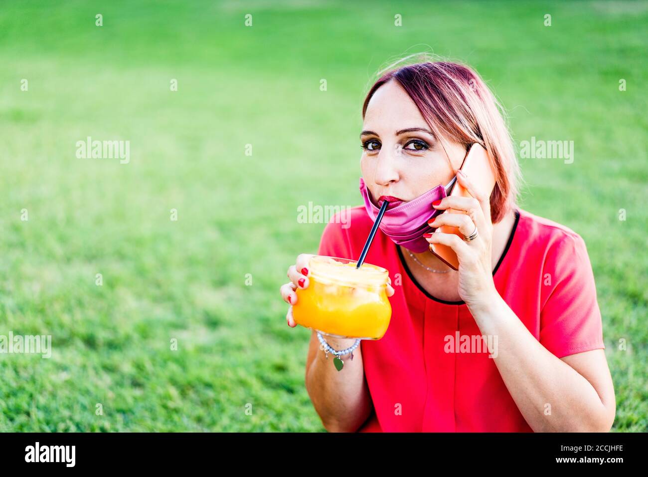 Woman with red lipstick and rose dyed hair drinking orange juice from ...