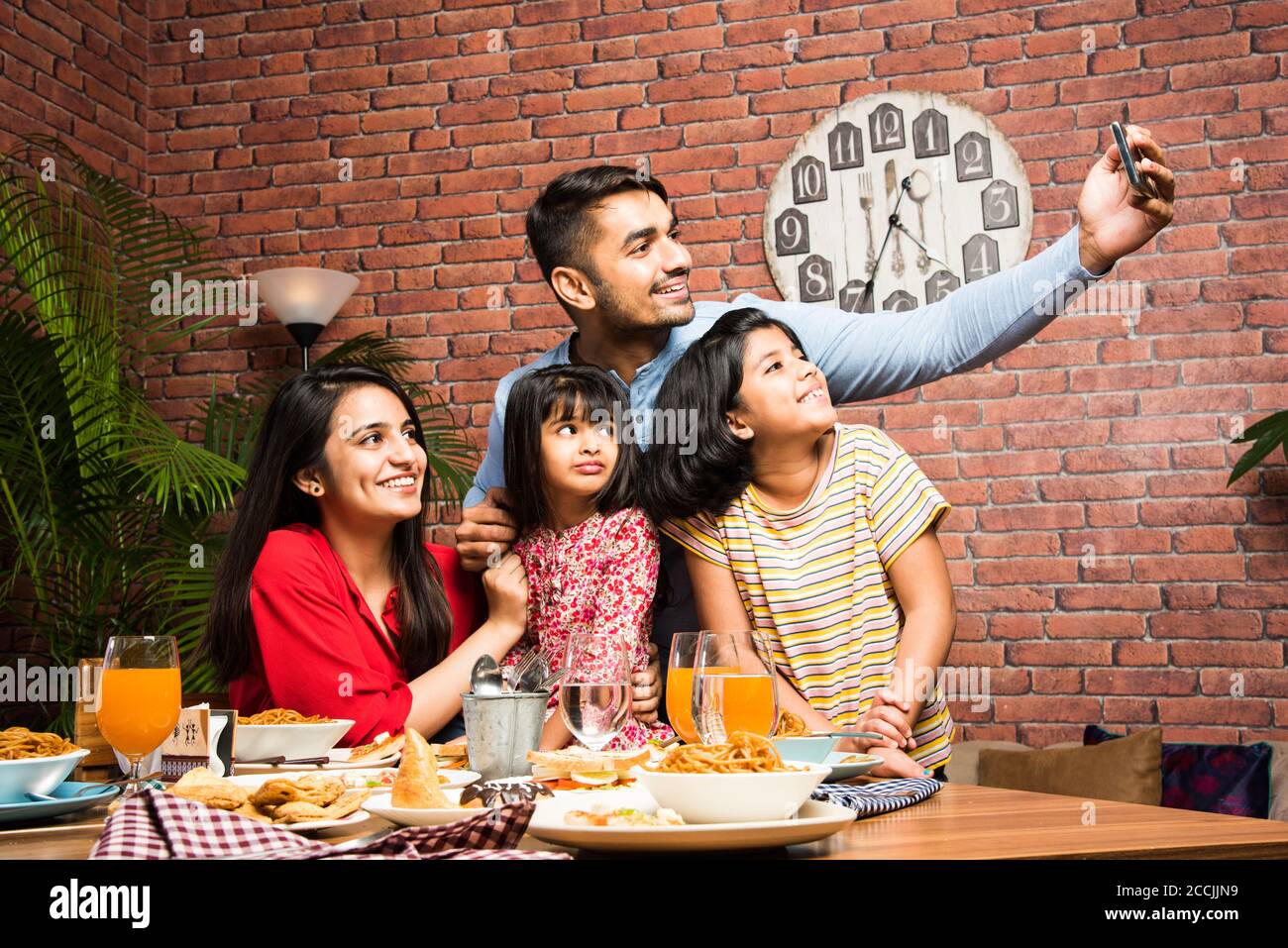 Indian young Family of four eating food at dining table at home or in ...