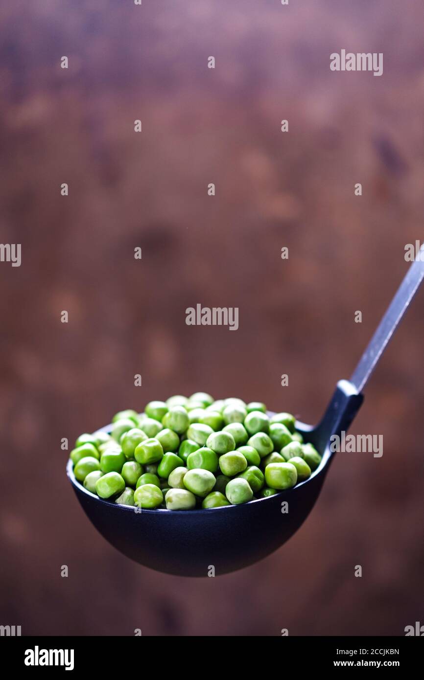 Fresh raw peas in a kitchen ladle over a mottled brown background with ...
