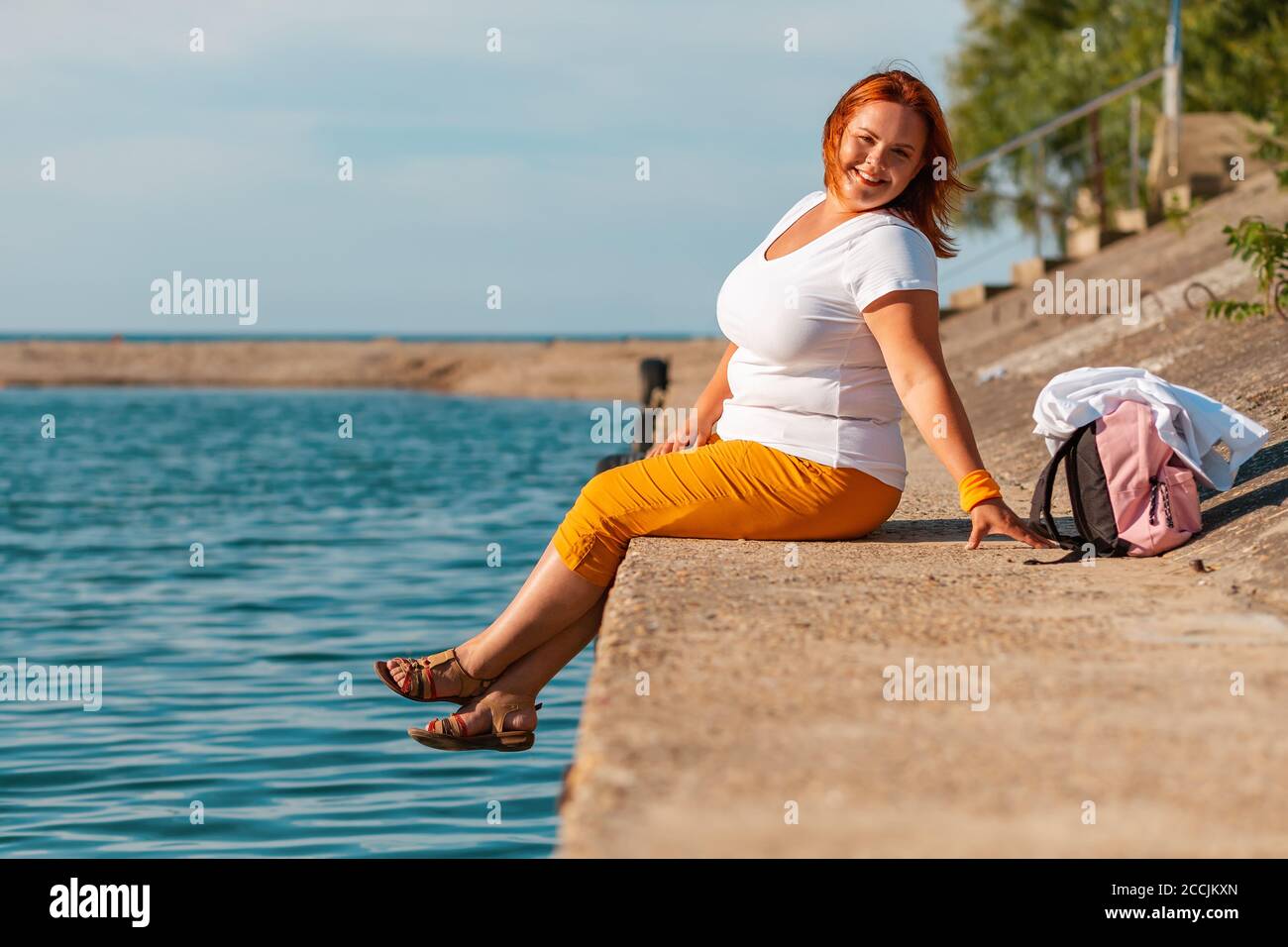 A happy overweight woman poses while sitting on a sea pier. Copy space ...
