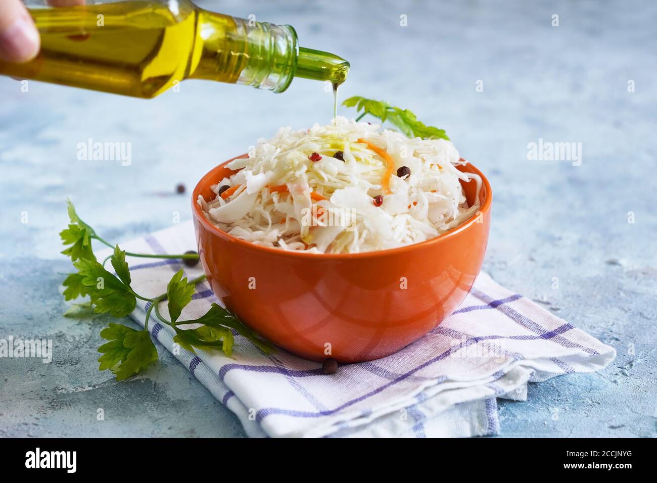 Female hand sprinkles olive oil on sauerkraut in a bowl. Healthy ...