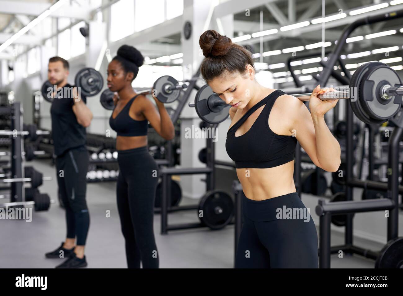 multiethnic group of people do exercises with barbells in gym ...