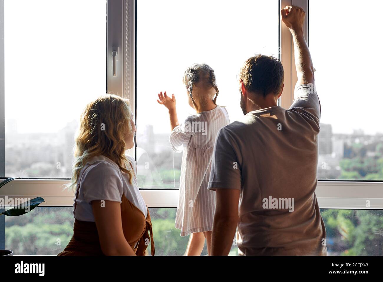 rear view on young family with child girl looking through the window at ...