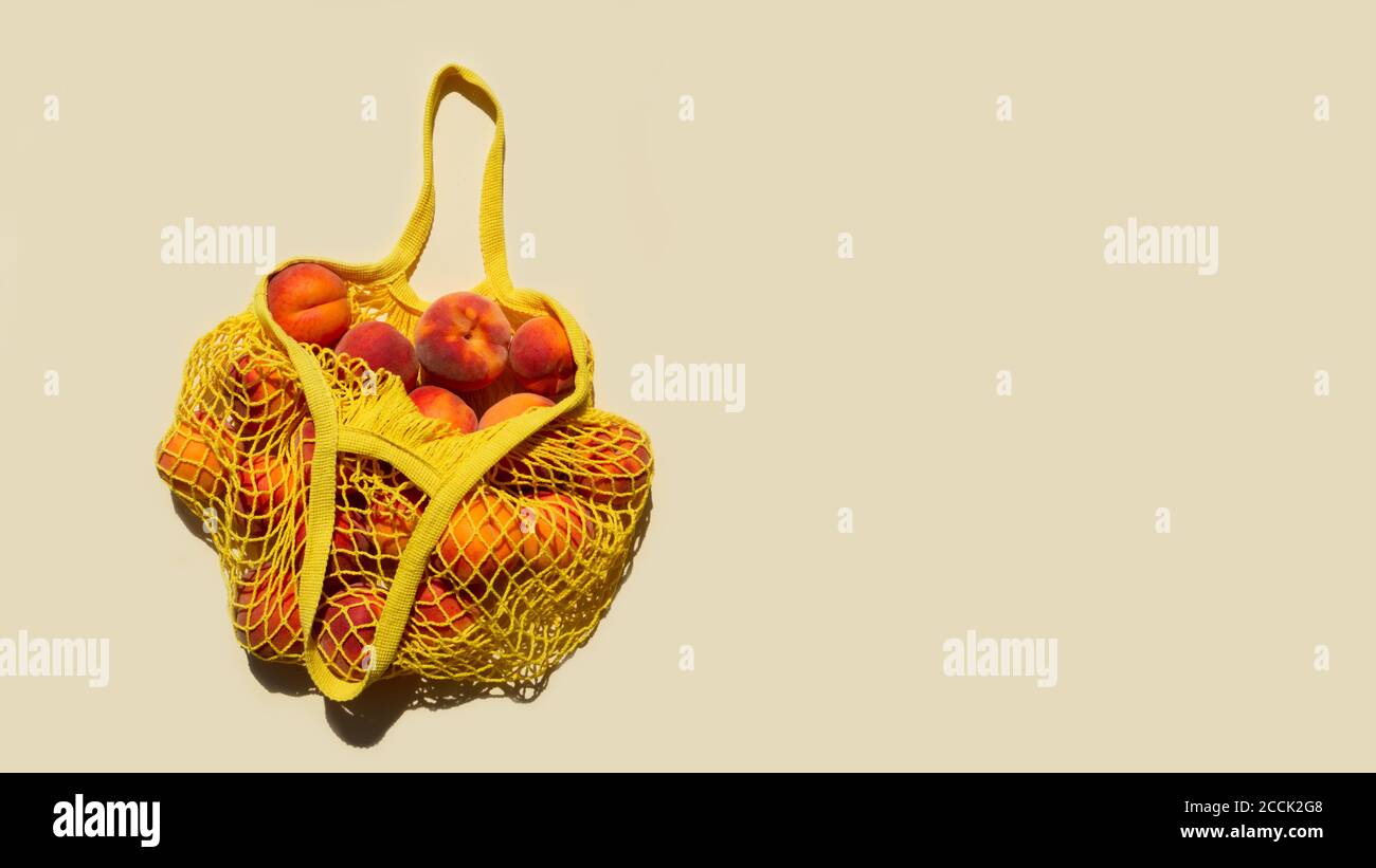 Ripe peaches in a mesh bag or string bag on light yellow background ...