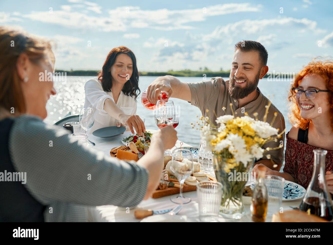 Friends having dinner at a lake drinking wine Stock Photo - Alamy