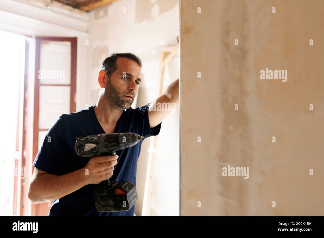 Construction worker using drill at a wall Stock Photo - Alamy