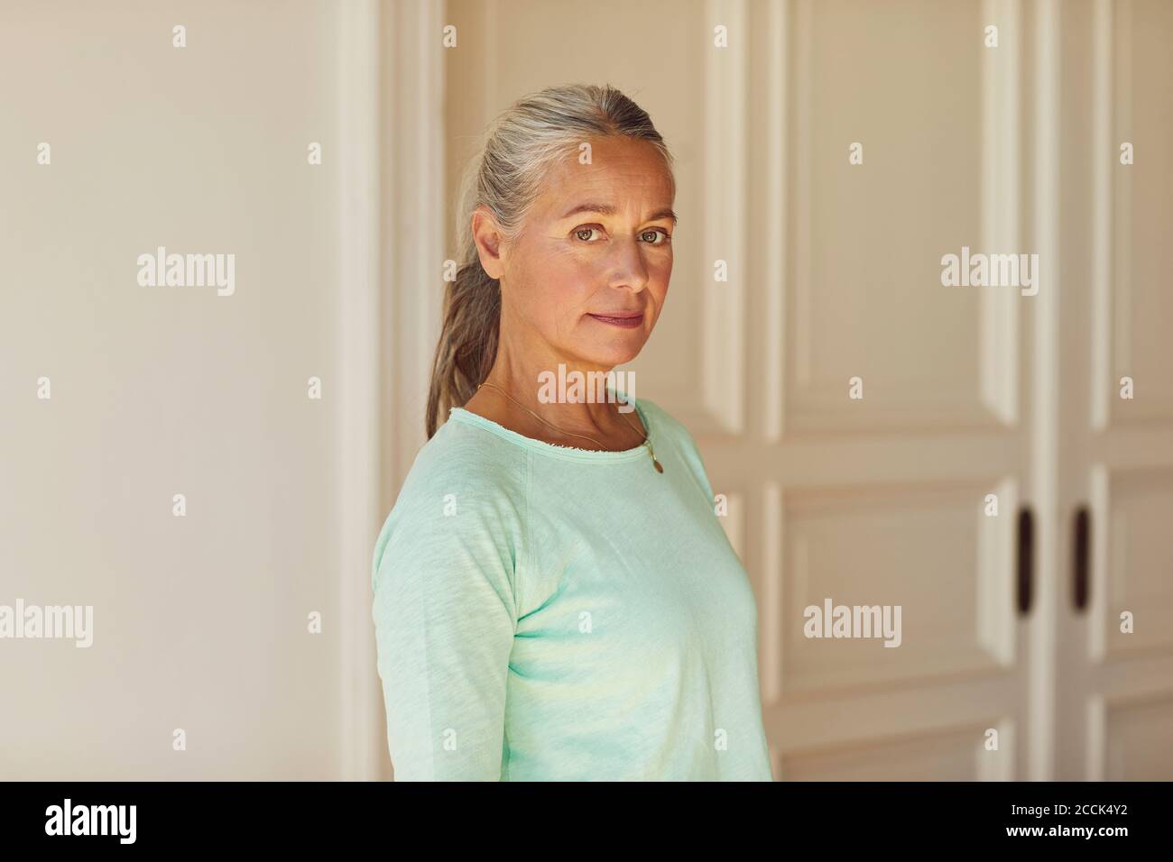 Thoughtful woman standing against door at home Stock Photo - Alamy