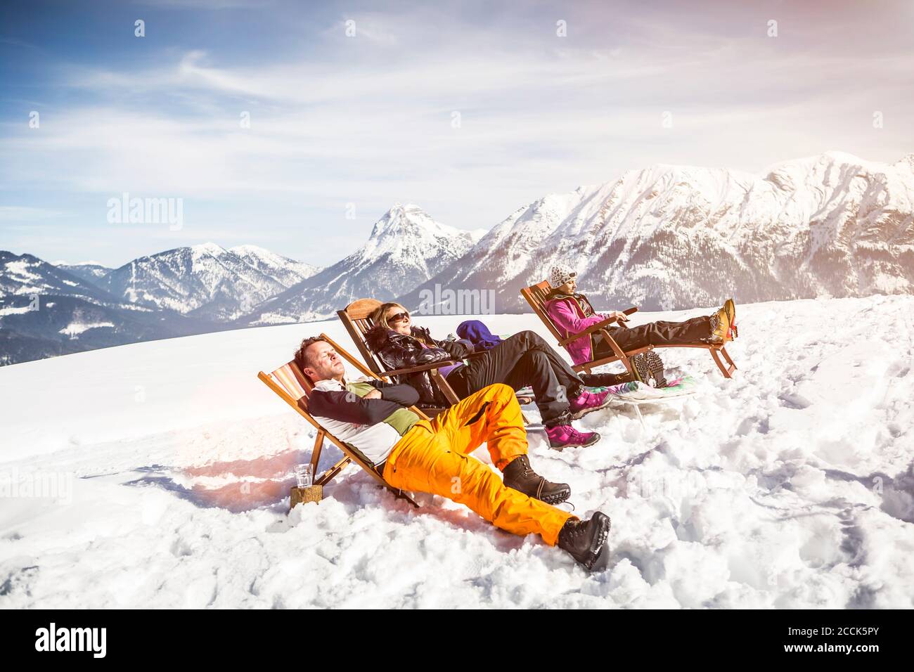 Friends sunbathing in deck chairs in mountainscape in winter ...
