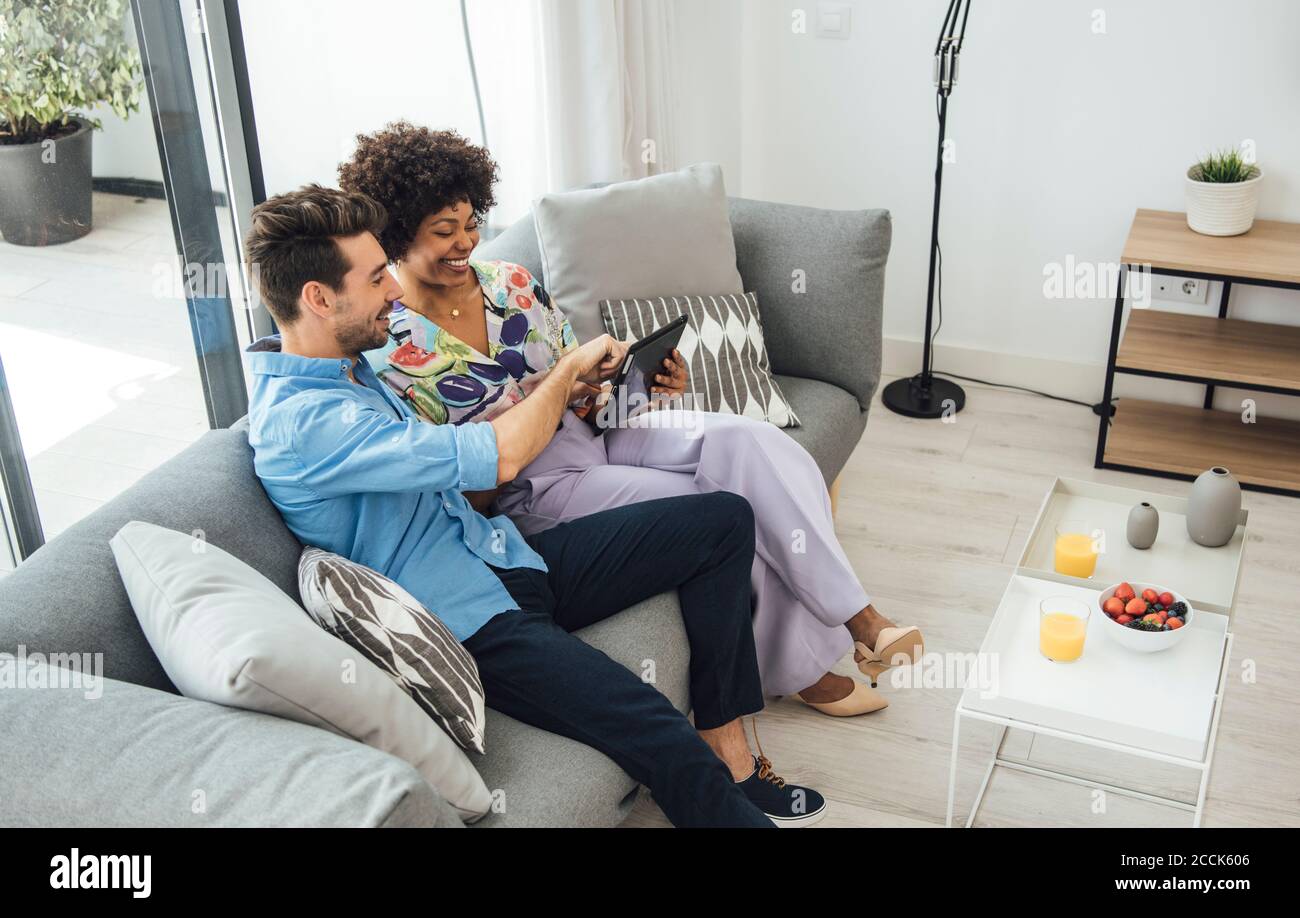 Happy couple using digital tablet while sitting on sofa in penthouse Stock Photo - Alamy