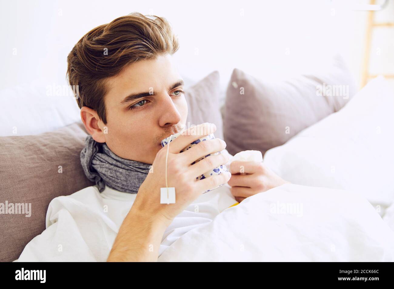 Close-up of sick young man having drink while resting on bed at home ...