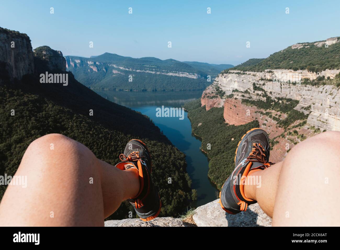 Legs of man sitting on mountain against clear sky at Vilanova de Sau ...