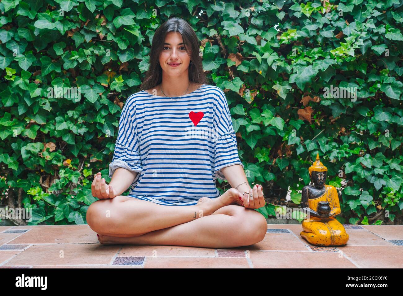 Young woman meditating by Buddha sculpture in backyard Stock Photo - Alamy