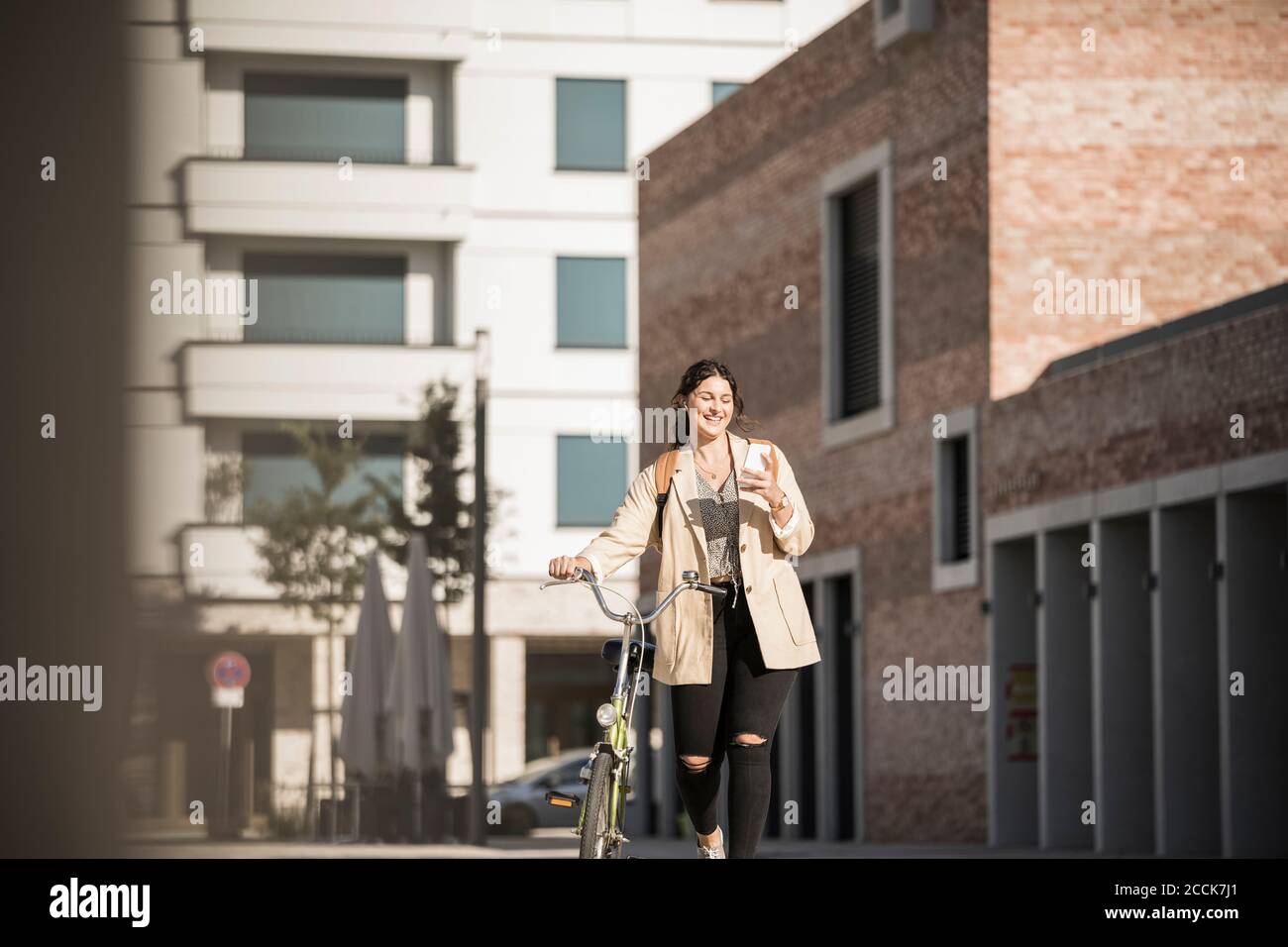 Female commuter using smart phone while walking with bicycle on city ...