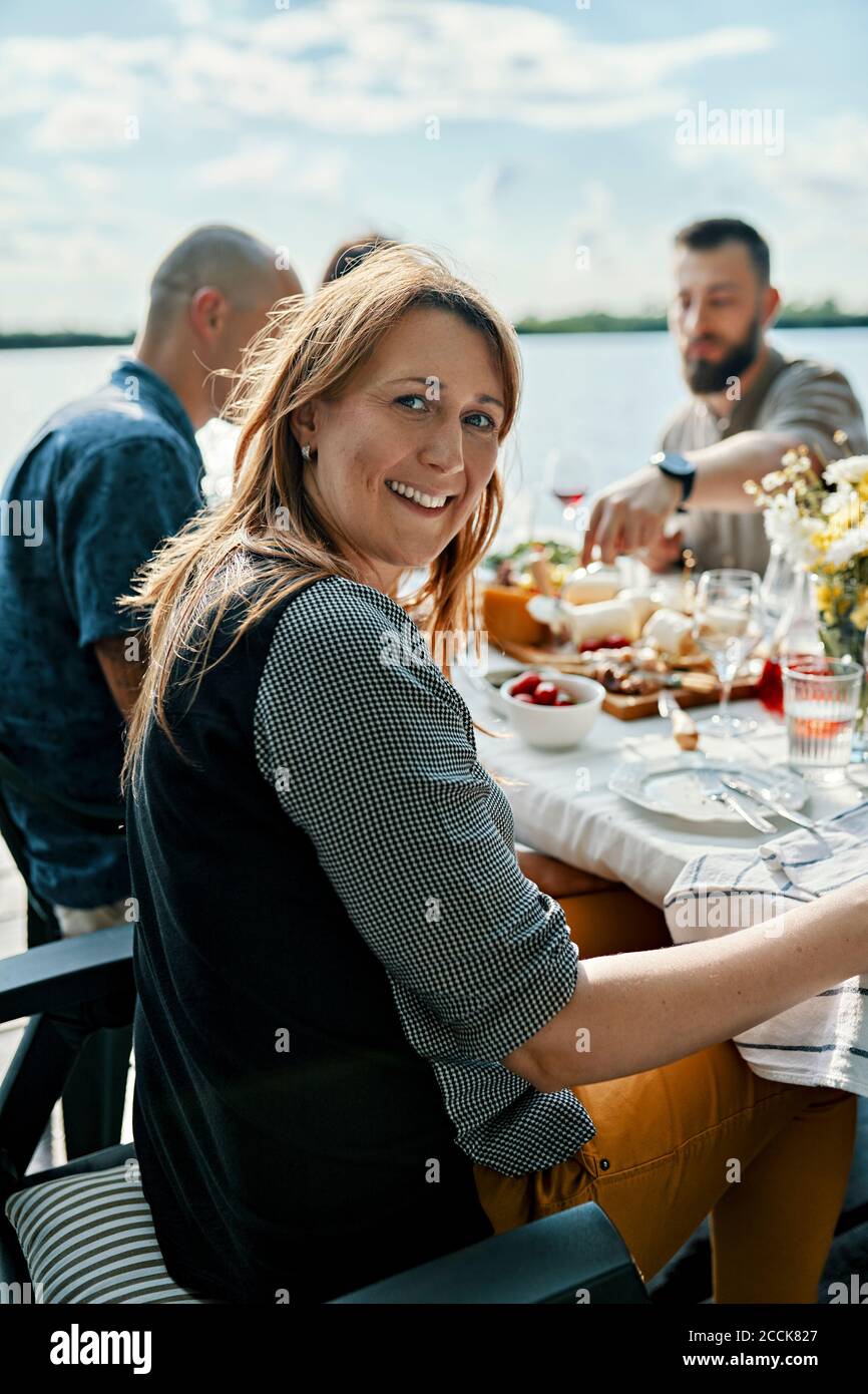 Portrait of smiling woman having dinner with friends at the lakeside ...