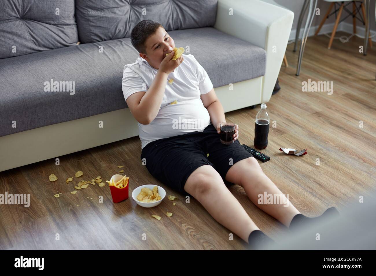 overweight fat boy eat junk food while watching tv alone at home, sit ...