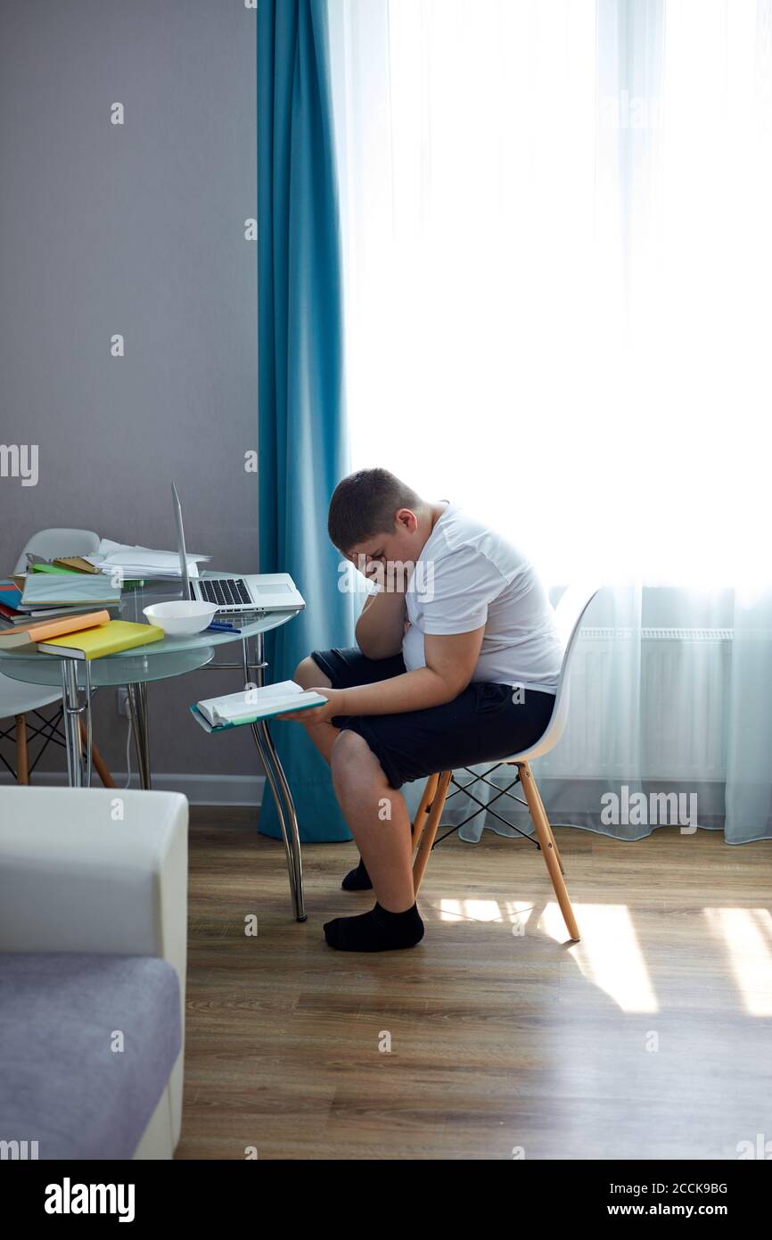 overweight boy tired of studying and doing homework, want to have rest ...
