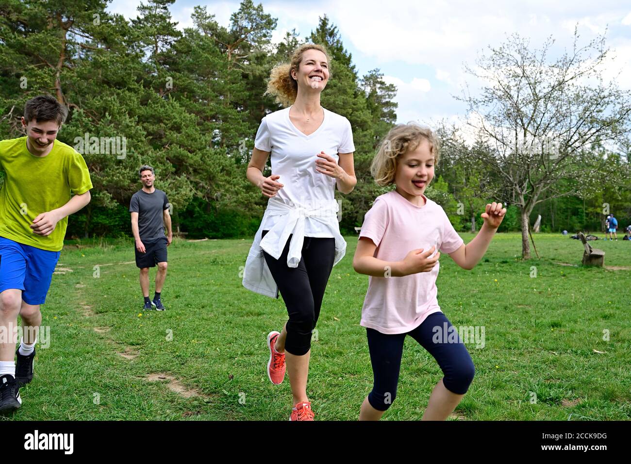 Happy family running on grassy land against trees in forest Stock Photo ...