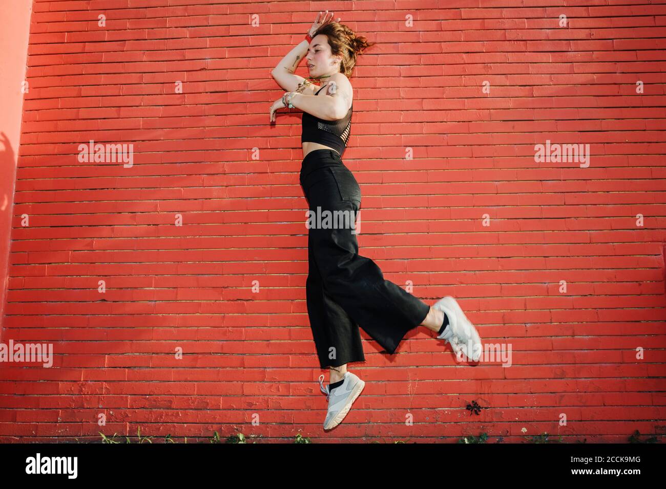 Woman jumping against red brick wall Stock Photo - Alamy