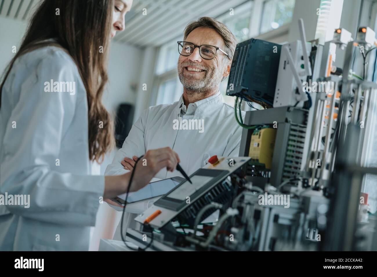 Smiling man looking at female colleague using machinery in laboratory ...
