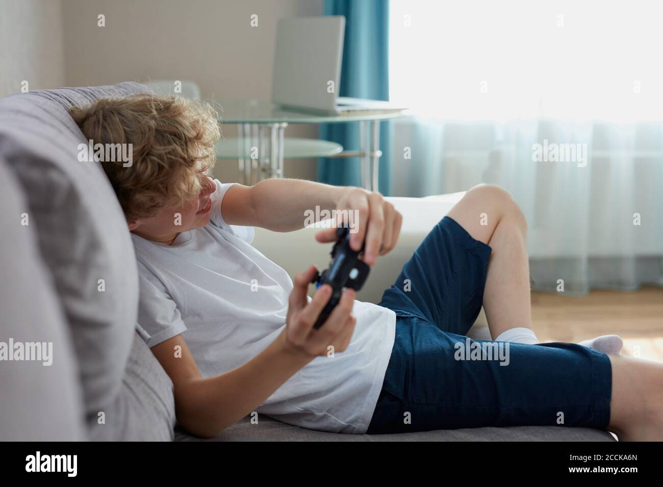 playful teenager keen on video games, sit on sofa in living room ...