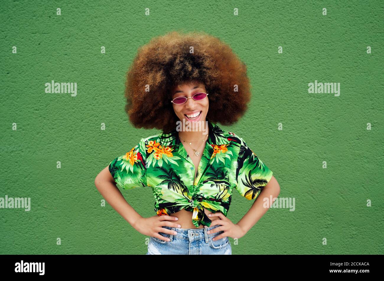 Smiling young woman in front of green wall Stock Photo - Alamy