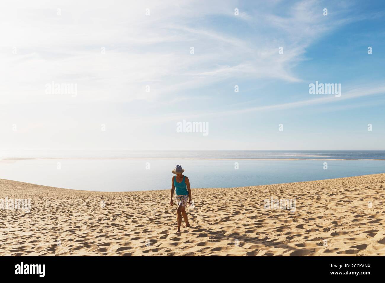 Woman walking on sand dunes at beach against sky hi-res stock ...