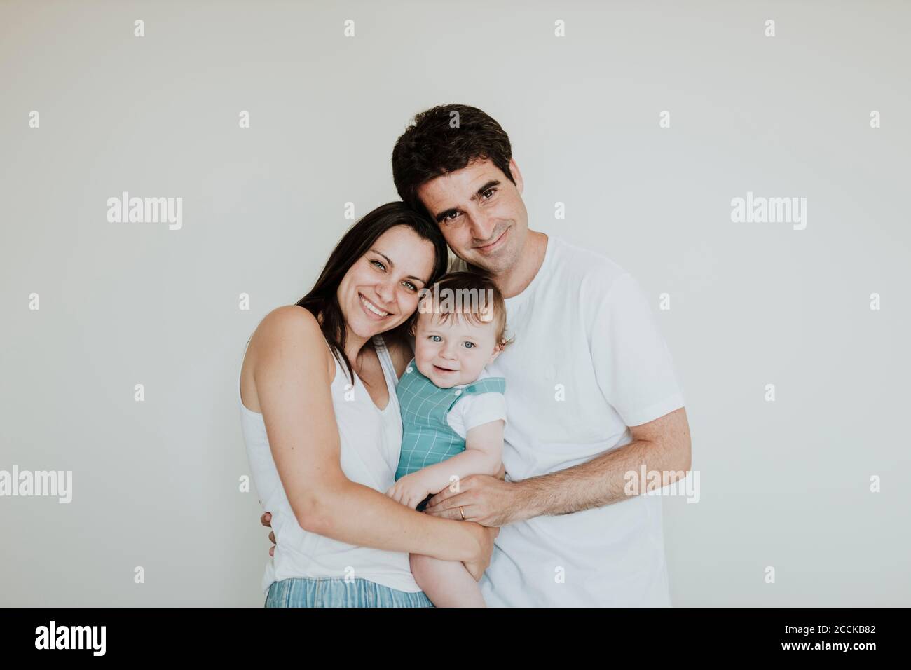 Parents carrying cute baby daughter while standing against white wall ...