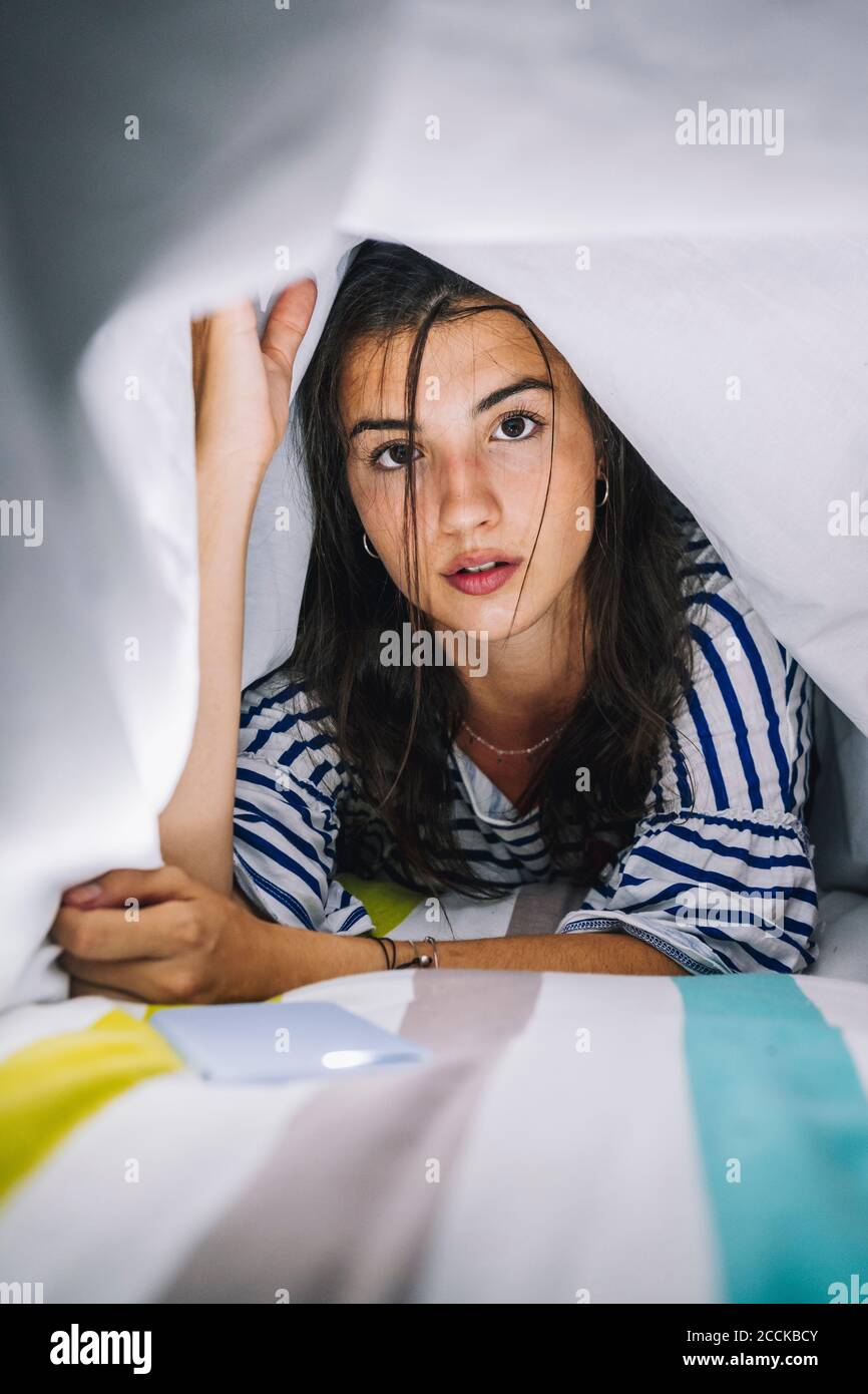 Beautiful young woman lying under blanket on bed Stock Photo - Alamy