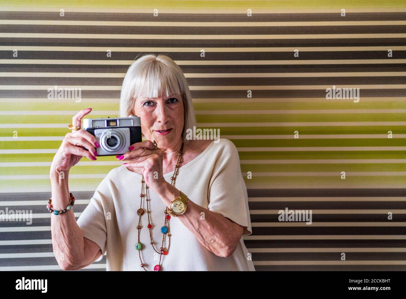 Stylish senior woman photographing with camera while standing against ...