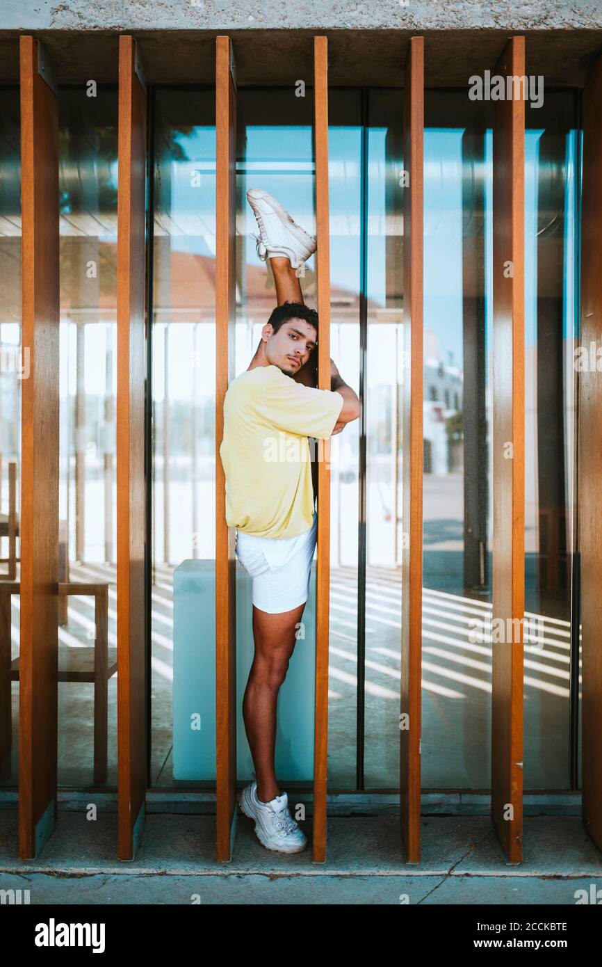 Confident young man doing rhythmic gymnastics exercise amidst wooden ...