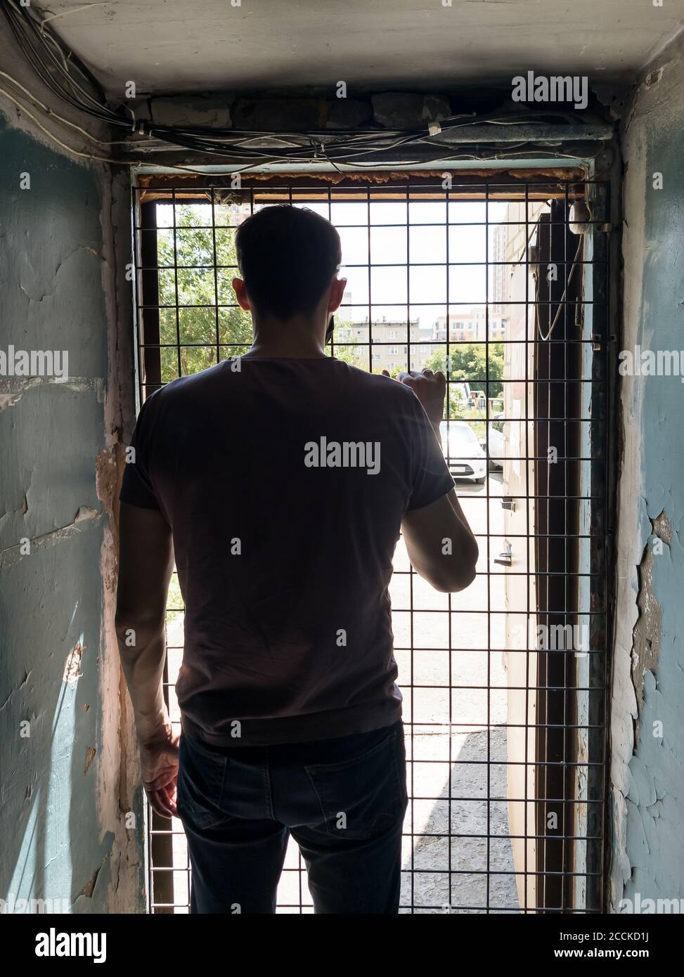 A back view of a man standing near a grate in the corridor of a prison ...