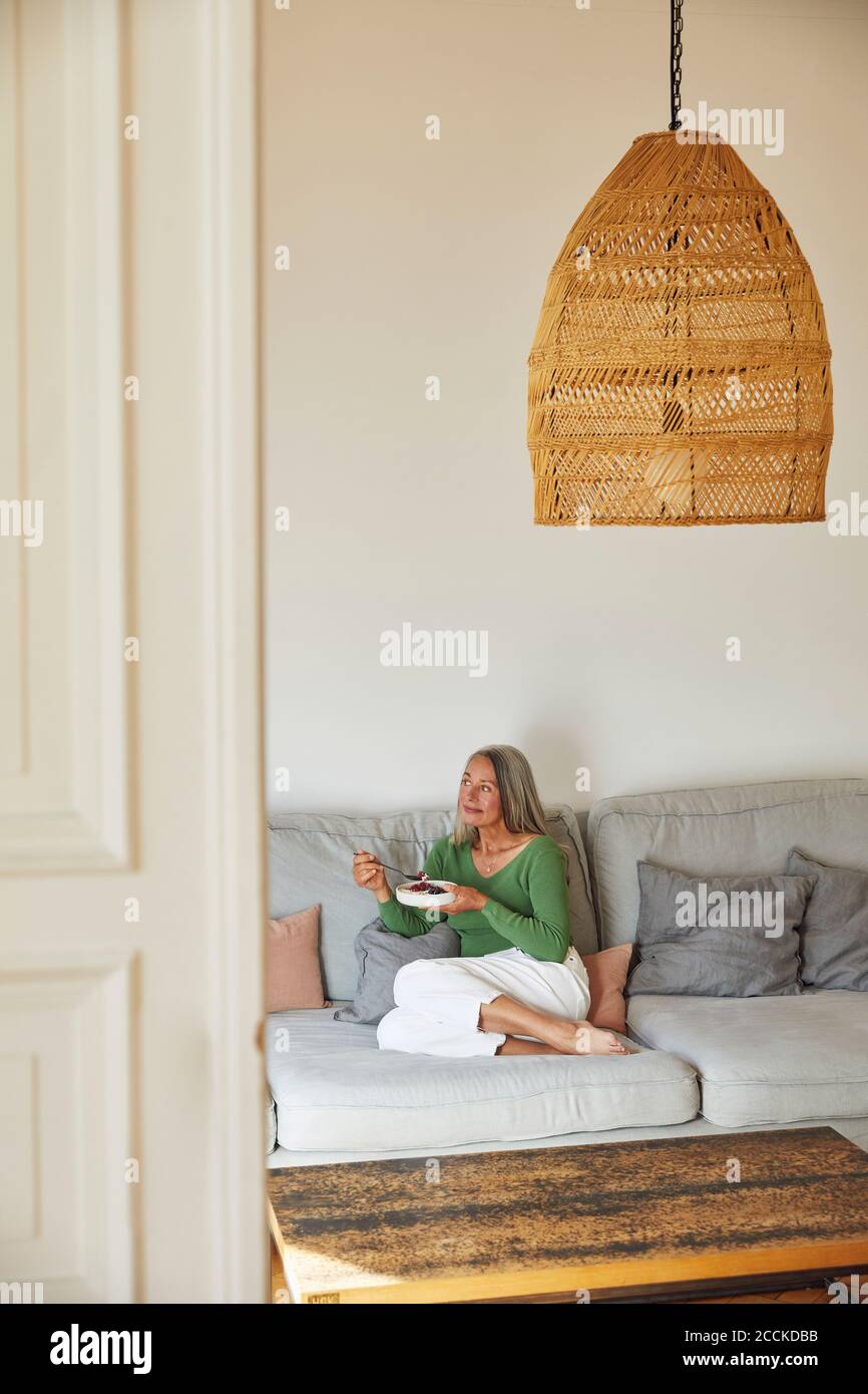 Woman eating breakfast while sitting on sofa at home Stock Photo - Alamy