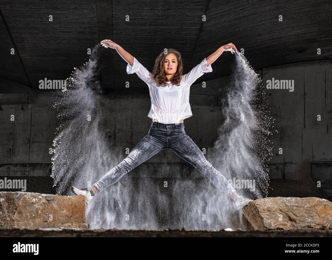 Young woman throwing flour while standing with legs apart on rocks ...